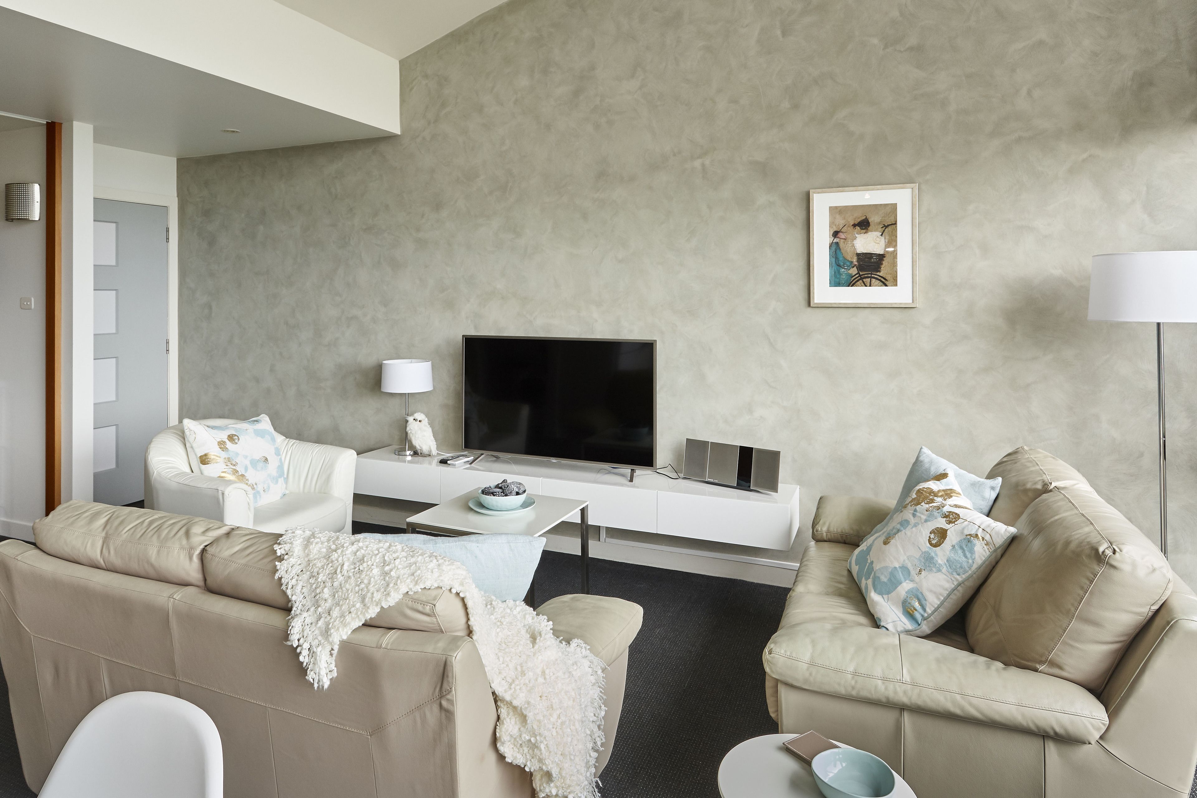 Uma sala de estar moderna com uma televisão de tela plana, um sofá branco, um sofá bege e uma mesa de centro.