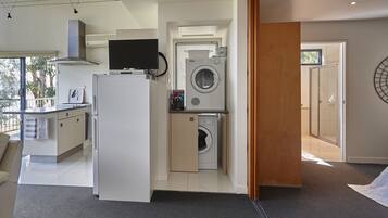 Cozinha compacta com máquina de lavar e secar integradas, televisão de tela plana e uma pequena ilha com pia e bancada.