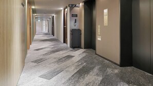 Um corredor de hotel com piso de carpete, portas com os números 4 e 5, e um elevador à direita.