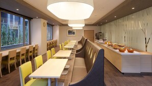 Restaurante moderno com mesas e bancos compridos, amplas janelas e um balcão central repleto de alimentos.