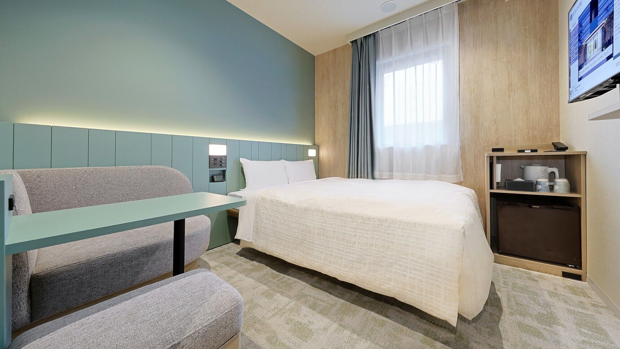 Quarto de hotel com cama, escrivaninha, cadeira, televisão e um pequeno armário.
