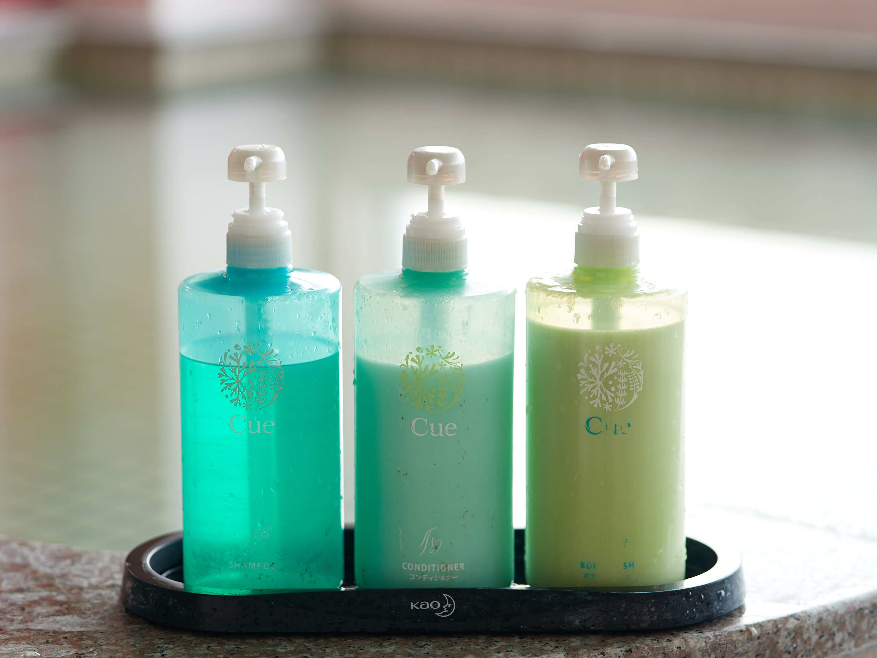 Três embalagens de shampoo e condicionador 'Cue' sobre um suporte preto.
