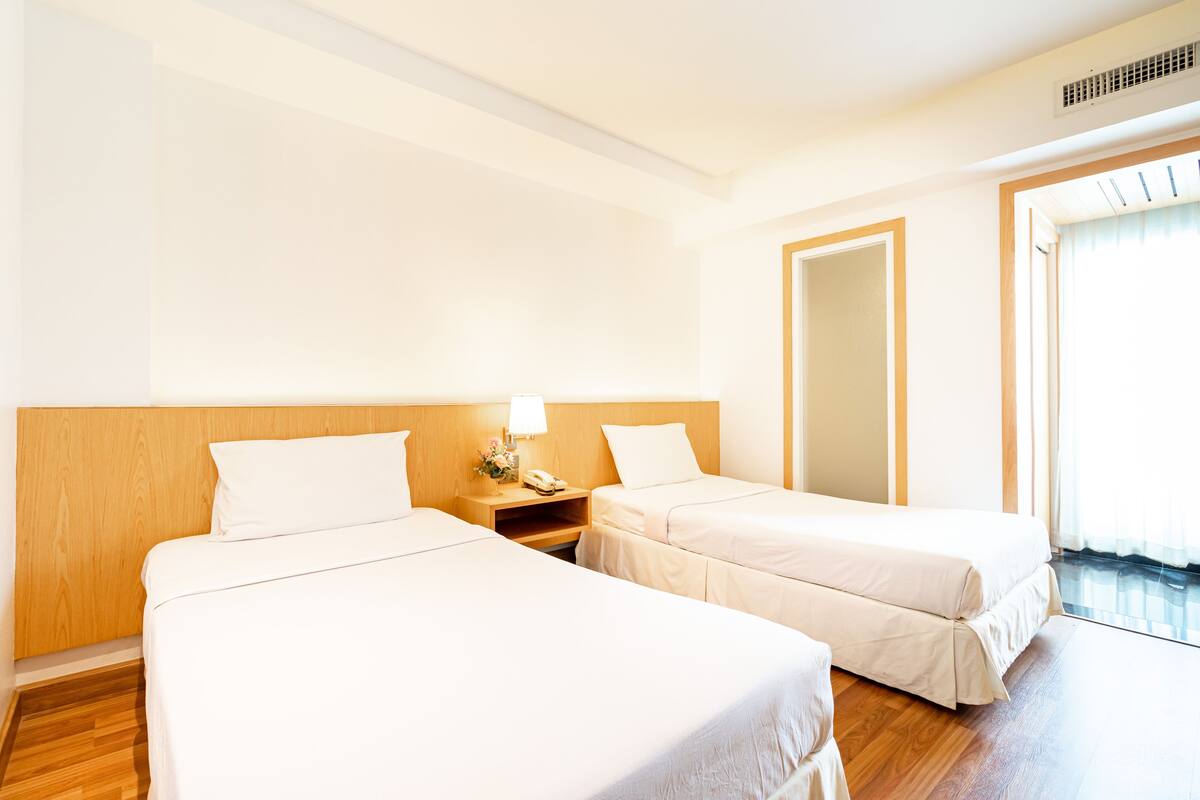 Quarto de hotel com duas camas de solteiro, cabeceira de madeira, mesa de cabeceira com luminária e um espelho grande.