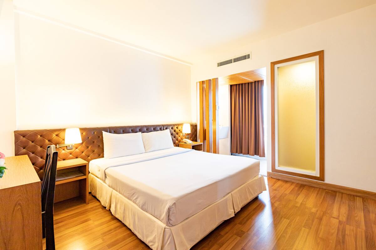 Quarto de hotel com uma cama grande, uma escrivaninha, uma cadeira, uma mesa de cabeceira e um espelho.