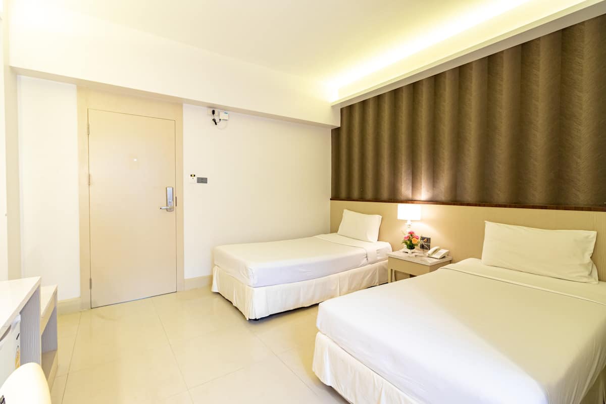 Quarto de hotel com duas camas, uma mesa de cabeceira com abajur, um telefone e uma porta.