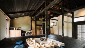 Um quarto amplo com piso de madeira, uma mesa central com tigelas e xícaras, e uma panela pendurada.