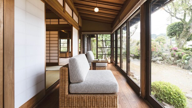 Um quarto tradicional em estilo japonês, com piso de tatame, teto de madeira baixo e grandes portas deslizantes que dão para um jardim.