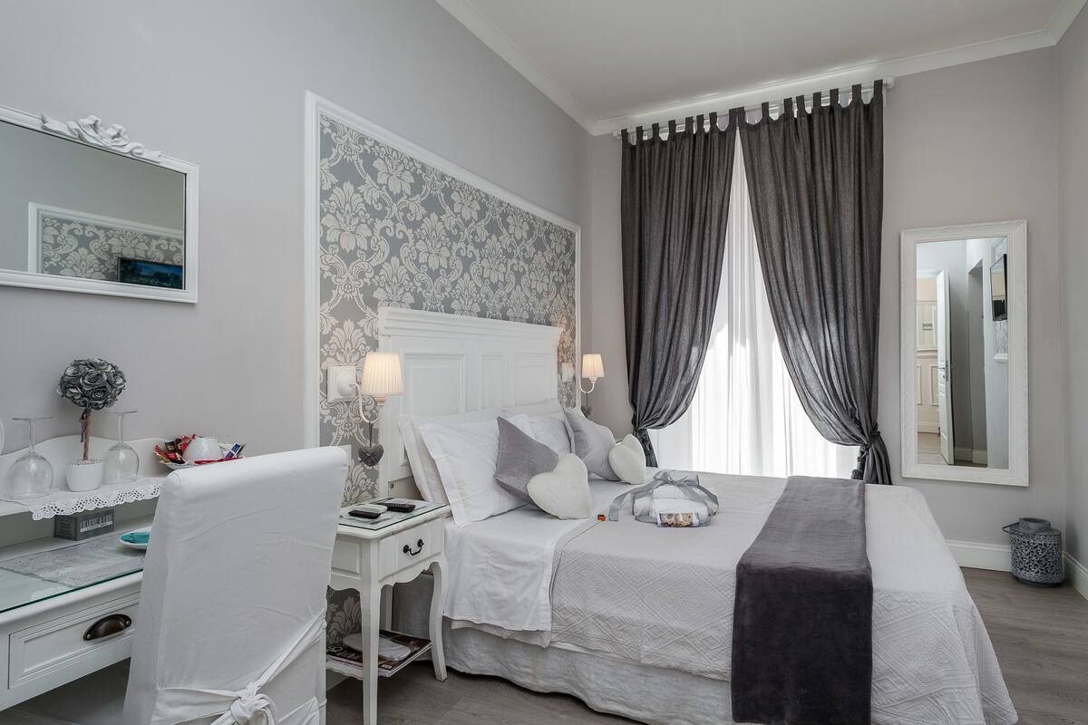 Quarto bem arrumado com cama, mesas de cabeceira, uma cadeira e cômoda.