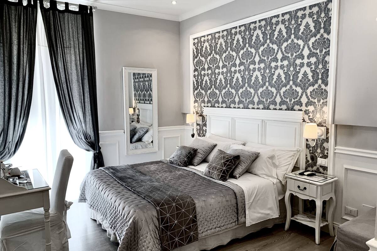 Quarto com cama grande, mesas de cabeceira, espelho e papel de parede estampado.