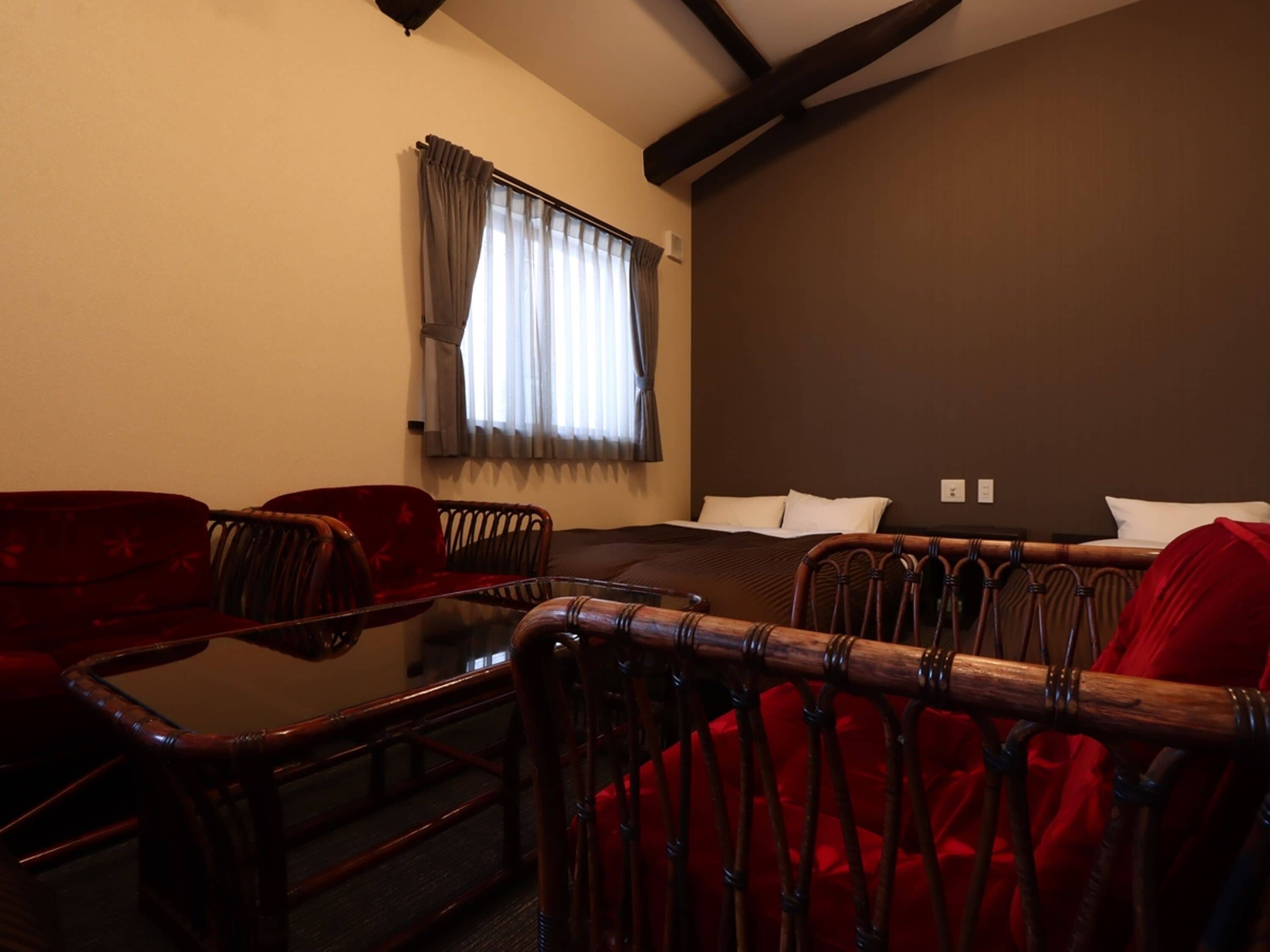 Quarto de hotel com cama, duas cadeiras, uma mesinha e janela com cortinas.