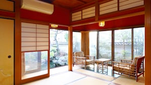 Um quarto japonês tradicional com tatames, portas deslizantes shoji e vista para um jardim através de grandes janelas.