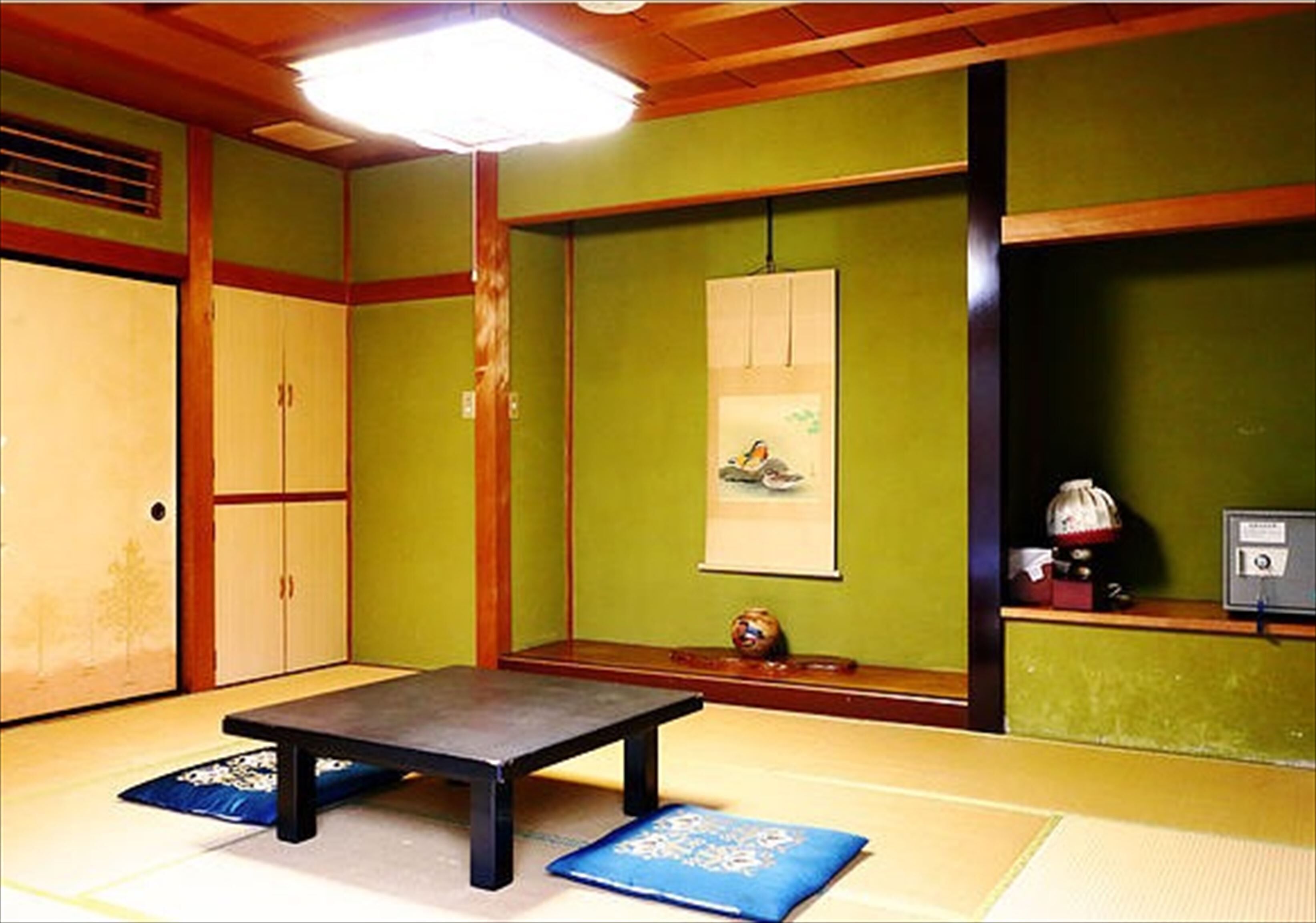 Um quarto com esteiras de tatame, uma mesa baixa, portas deslizantes e uma obra de arte tradicional japonesa na parede.