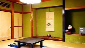 Um quarto com esteiras de tatame, uma mesa baixa, portas deslizantes e uma obra de arte tradicional japonesa na parede.
