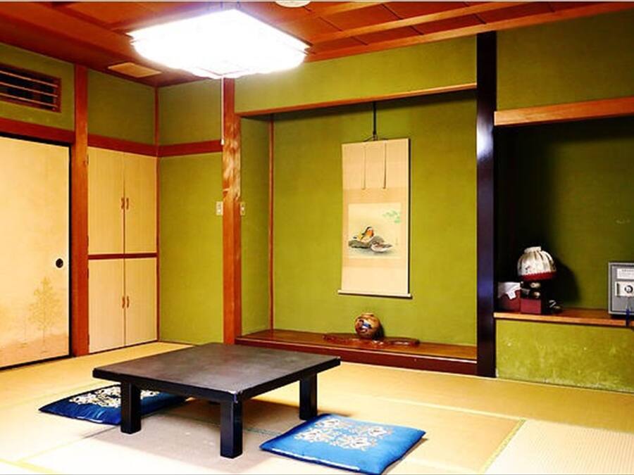 Um quarto com esteiras de tatame, uma mesa baixa, portas deslizantes e uma obra de arte tradicional japonesa na parede.