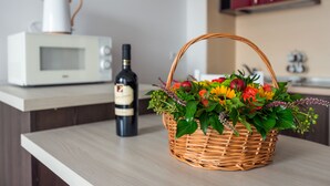 Uma bancada de cozinha com micro-ondas, uma garrafa de vinho e uma cesta de vime com produtos frescos.