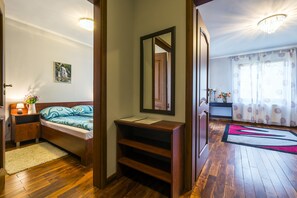 Quarto com cama de madeira, mesa de cabeceira, espelho e mesa auxiliar com abajur.