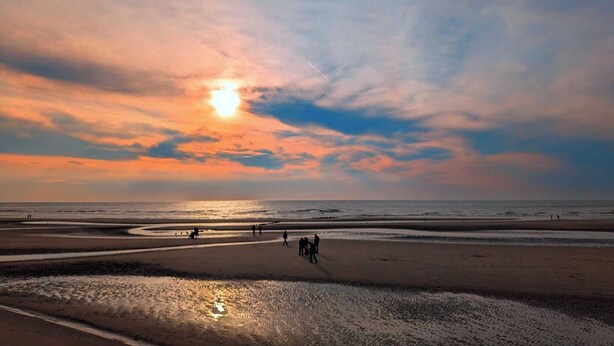 Cena de praia com pessoas caminhando pela costa ao pôr do sol.