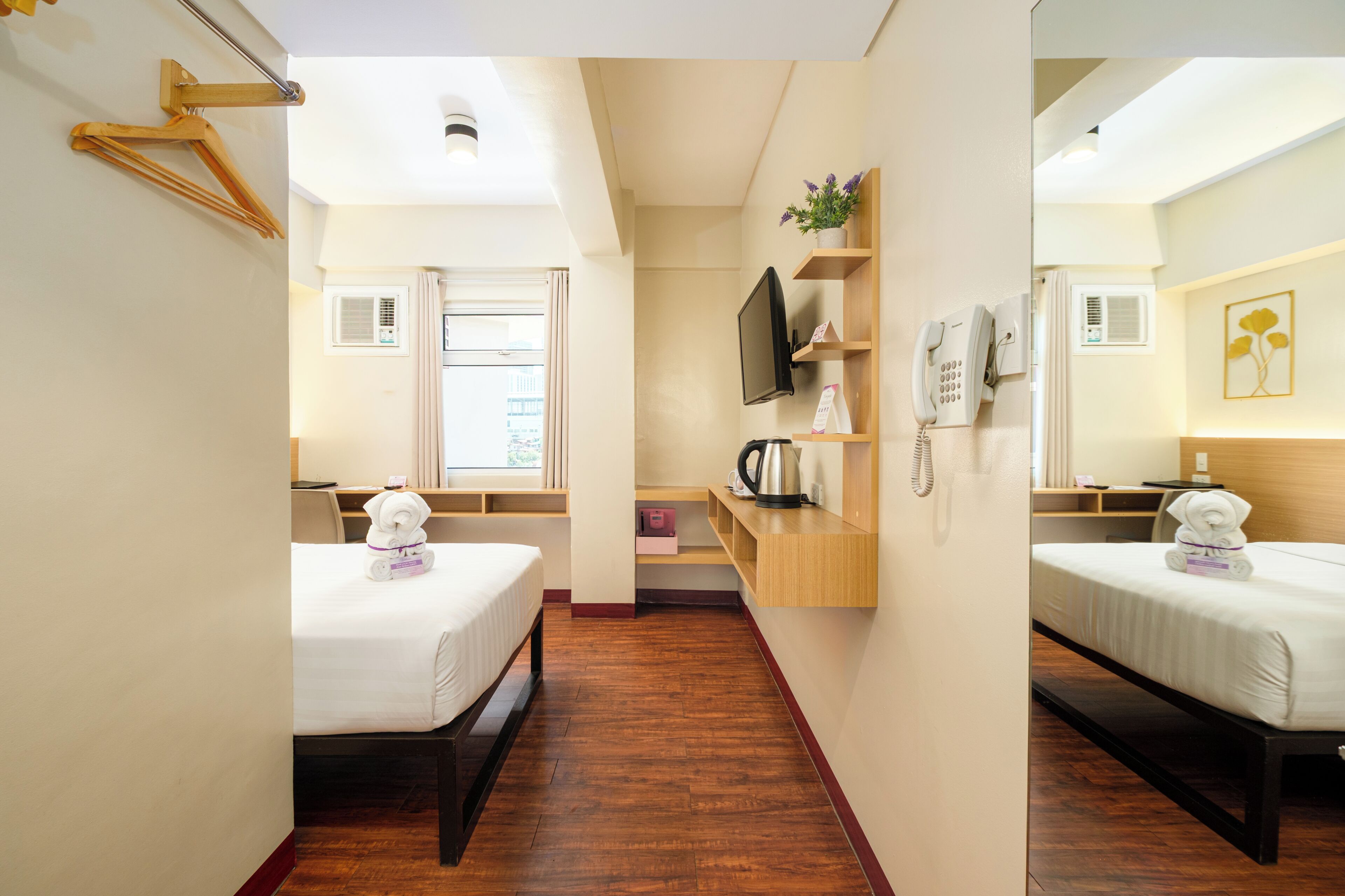 Quarto de hotel com duas camas, uma televisão, um telefone e uma estante com comodidades.