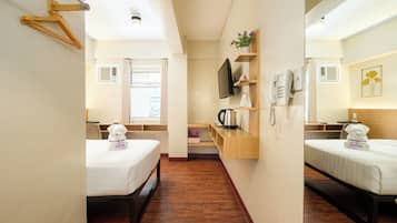 Quarto de hotel com duas camas, uma televisão, um telefone e uma estante com comodidades.
