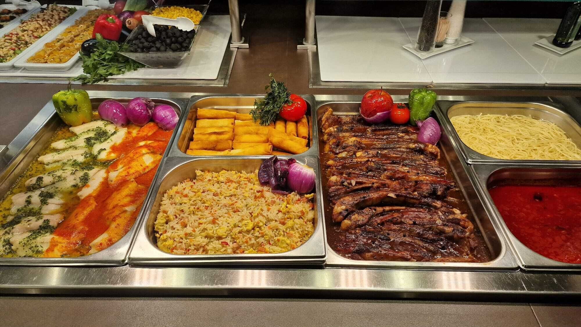Buffet com diversos pratos, incluindo peixes, arroz e carnes.