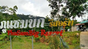 Placa indicando o Phu Sam Big Resort, com texto em tailandês e inglês, cercada por vegetação e um caminho.