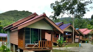 Uma fileira de cabanas de madeira com varandas, inserida em um ambiente verdejante, com uma montanha ao fundo.