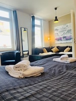 Quarto de hotel com cama, poltrona, sofá, espelho grande e pintura na parede.