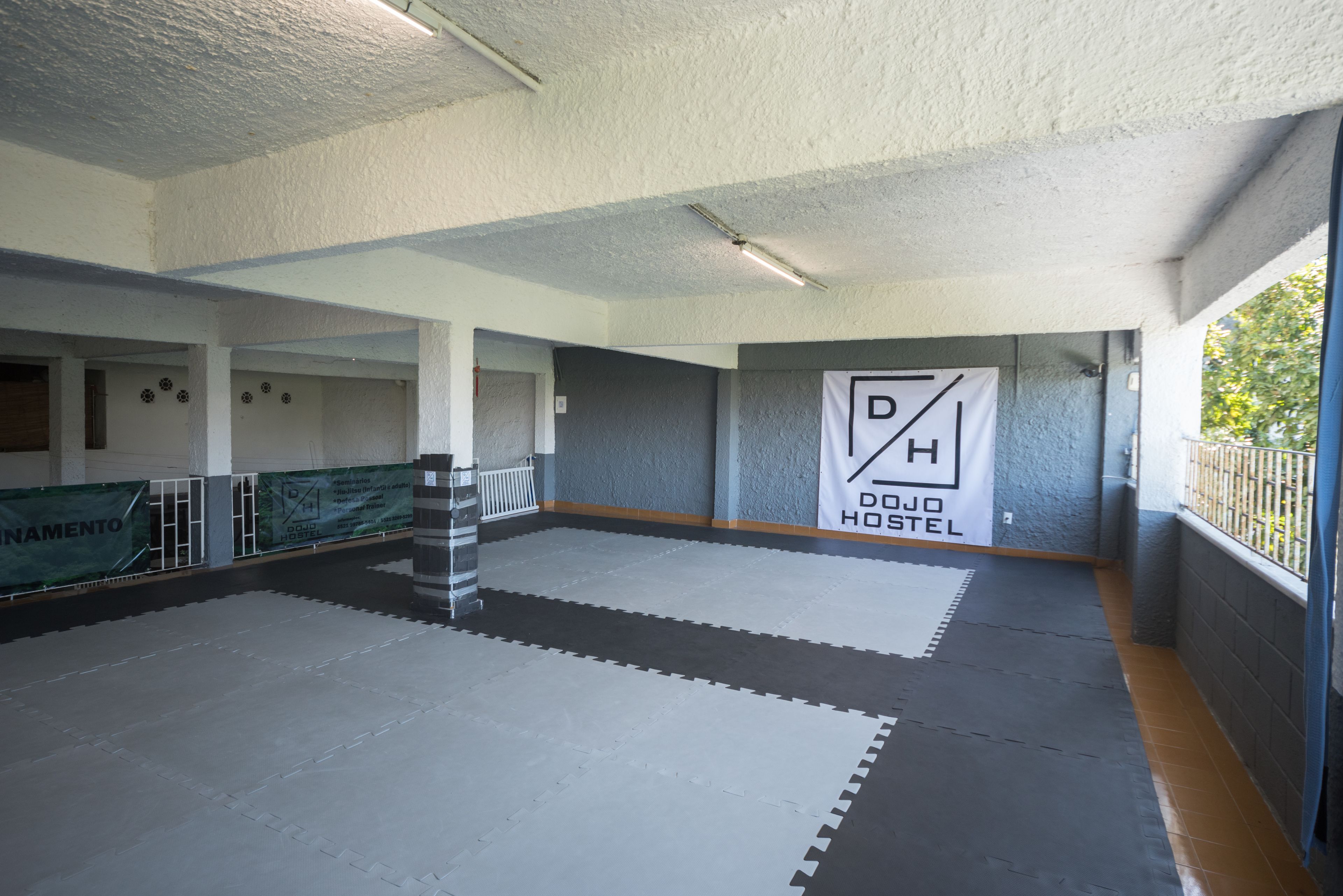Um espaço interno amplo com uma placa indicando "DOJO HOSTEL" e piso de azulejos.