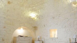 Quarto com parede de pedra, uma cama, cômoda e mesa de cabeceira.