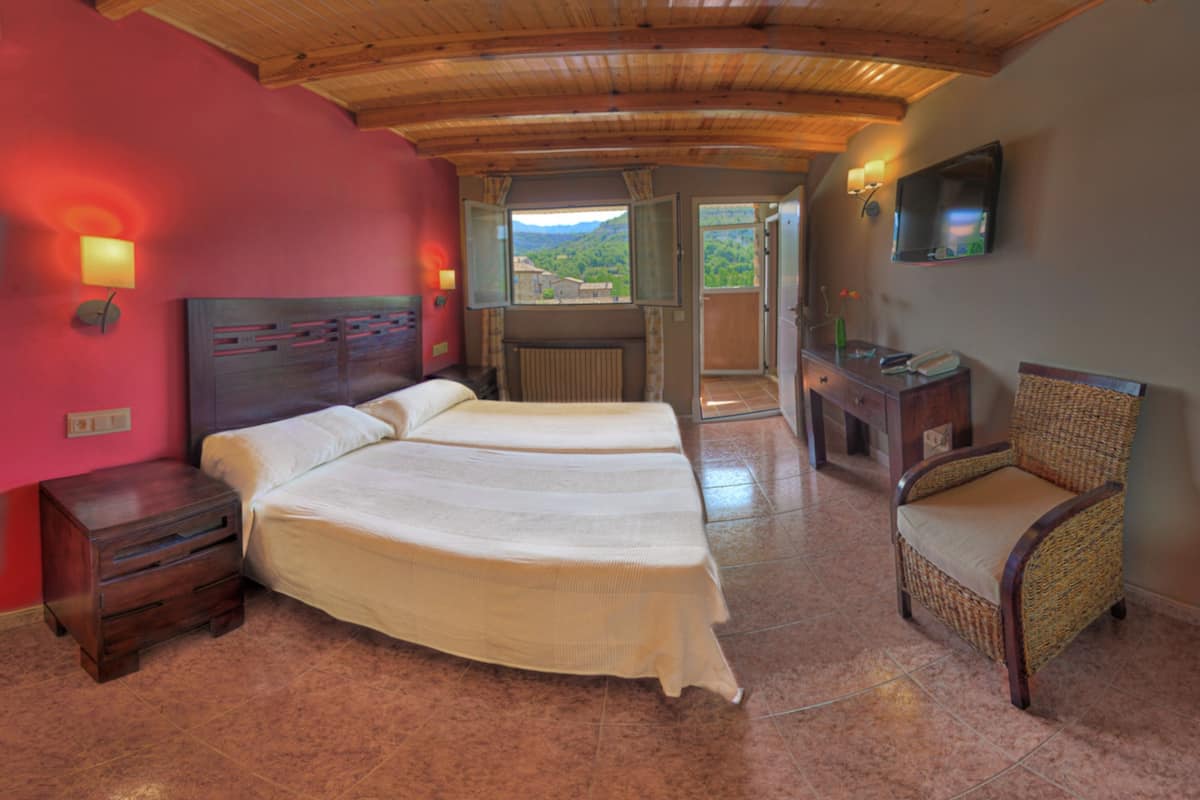 Quarto de hotel com duas camas, teto de madeira, televisão e vista para as montanhas.
