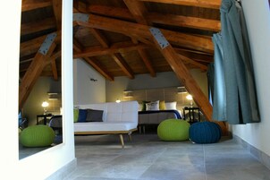 Quarto de sótão com teto inclinado, um sofá branco, dois pufes verdes e uma bola azul.