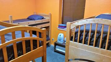 Quarto com três beliches de madeira, cada um com colchão e travesseiro azuis. Há um aquecedor sobre uma pequena mesa ao lado das camas.