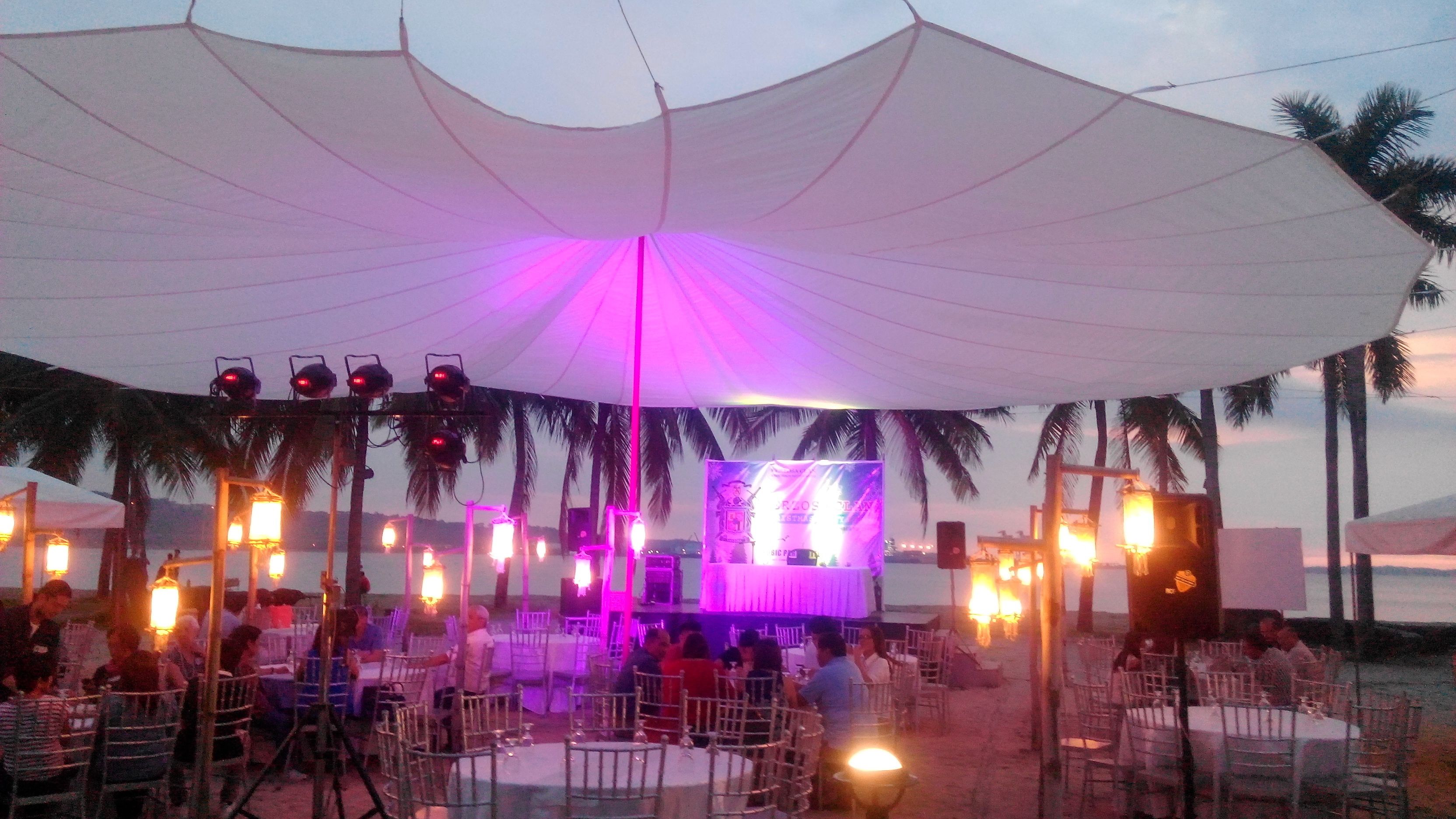 Evento ao ar livre com palco e mesas dispostas sob uma grande cobertura.