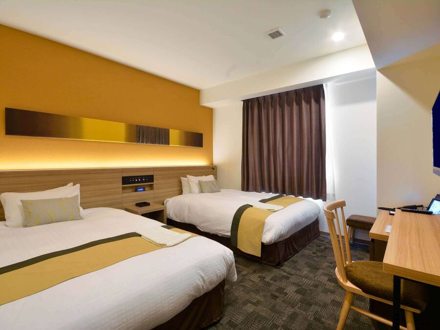 Quarto de hotel com duas camas, uma escrivaninha, uma cadeira e uma televisão.