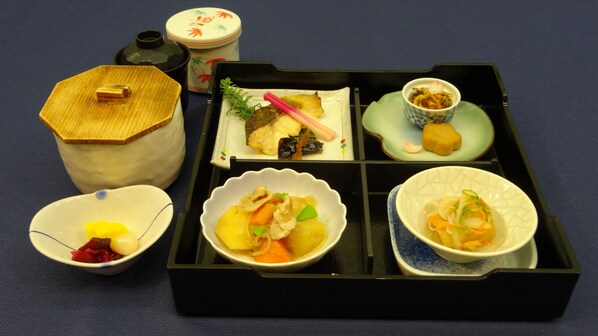 Uma tradicional caixa de bento japonesa com diversos pratos, incluindo peixe, legumes e uma pequena tigela de itens em conserva.