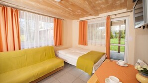 Quarto com teto de madeira, sofá amarelo, cama com cobertor verde e mesa com xícara e flores.
