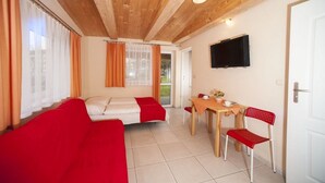 Quarto com teto de madeira, uma cama, sofá vermelho, mesa de jantar com cadeiras e televisão fixada na parede.