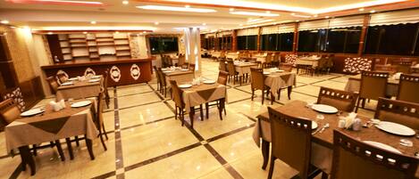 Um restaurante amplo com várias mesas e cadeiras, piso ladrilhado e ambiente bem iluminado.