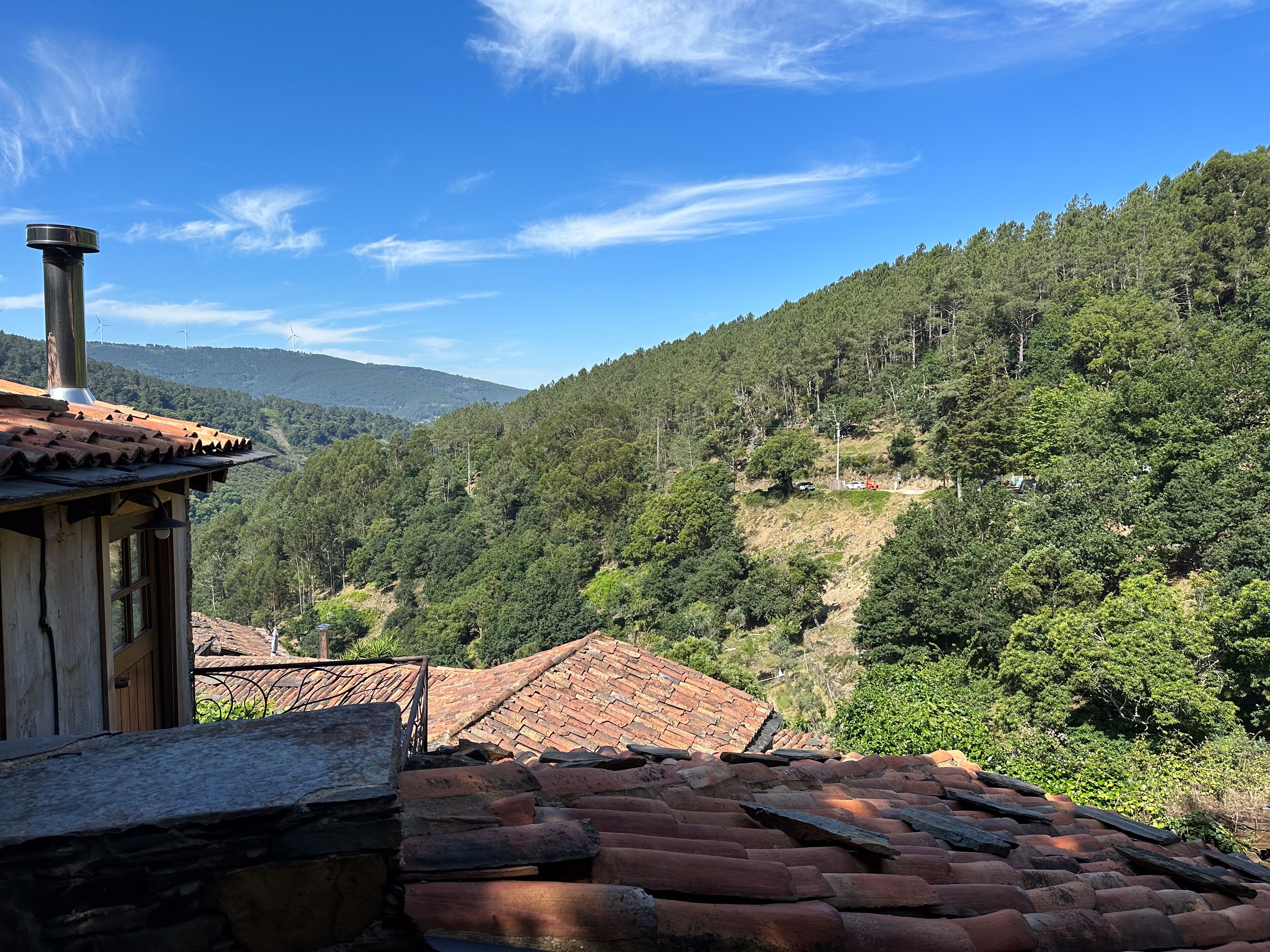 Um edifício rústico com telhado de cerâmica, com vista para uma encosta arborizada.