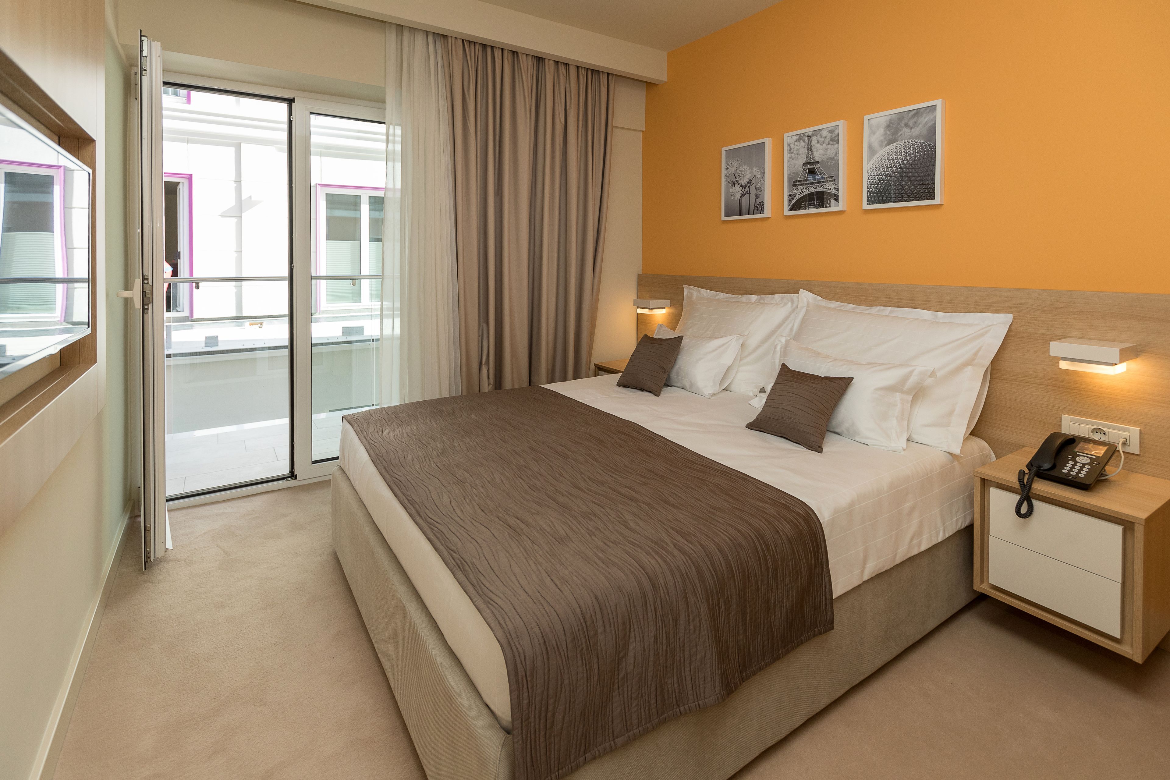 Quarto de hotel com uma cama, uma mesa de cabeceira com telefone e vista para o exterior por uma porta de correr.