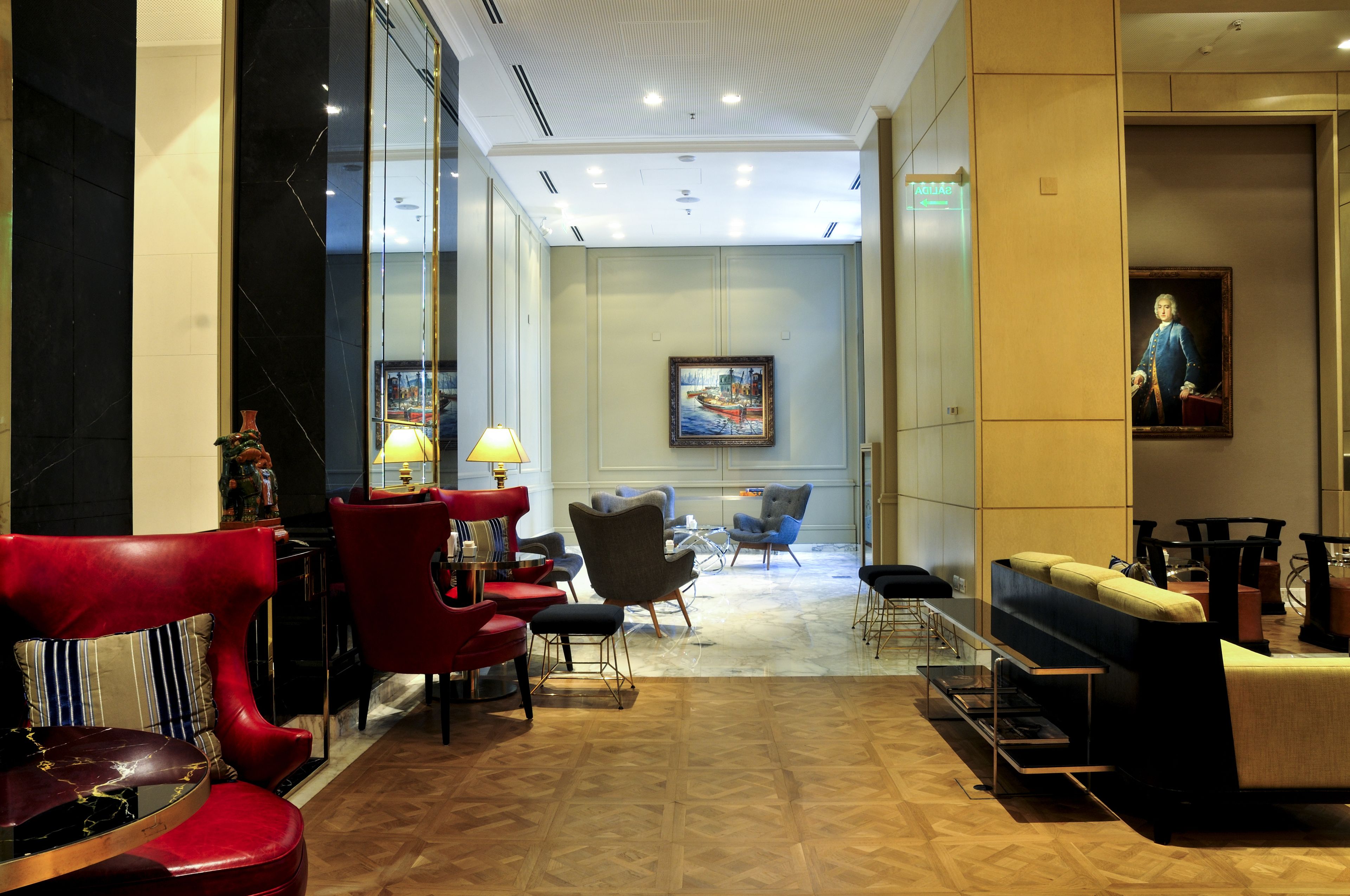 Um saguão de hotel com sofás de couro vermelho e preto, piso de madeira e uma pintura na parede.