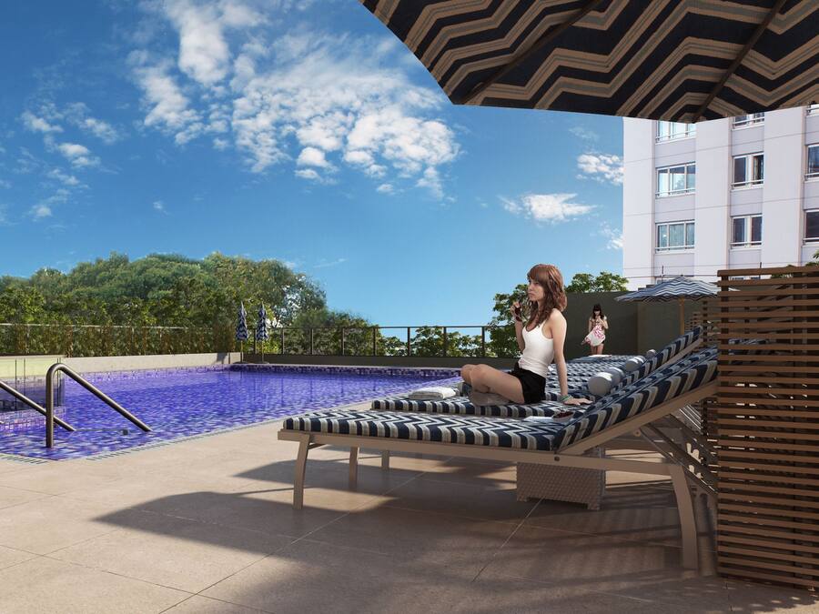 Uma área de piscina no terraço, com céu claro, piscina com azulejos azuis, espreguiçadeiras e um edifício ao fundo.