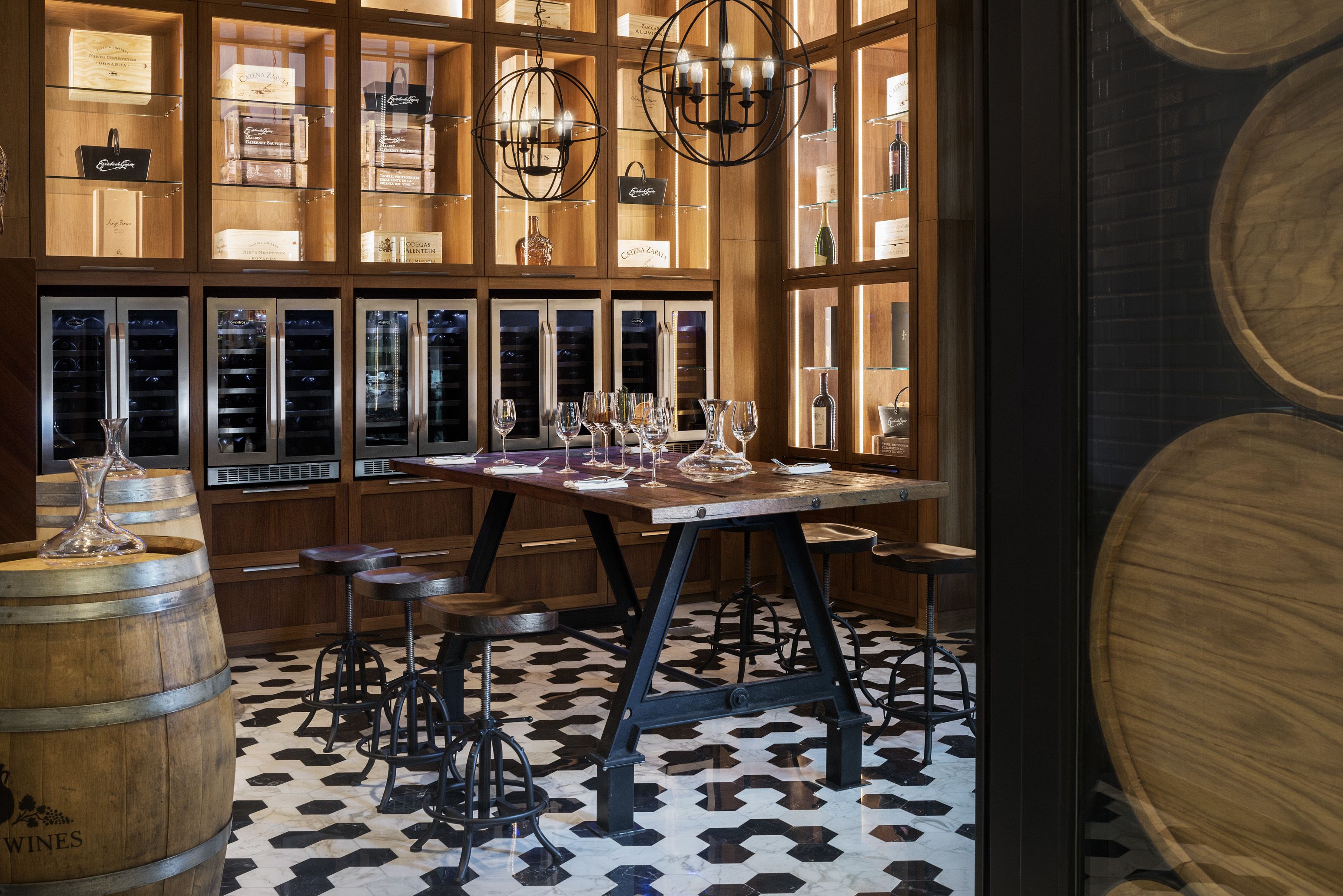 Uma área de bar com prateleiras de madeira, copos de vinho e banquetas.