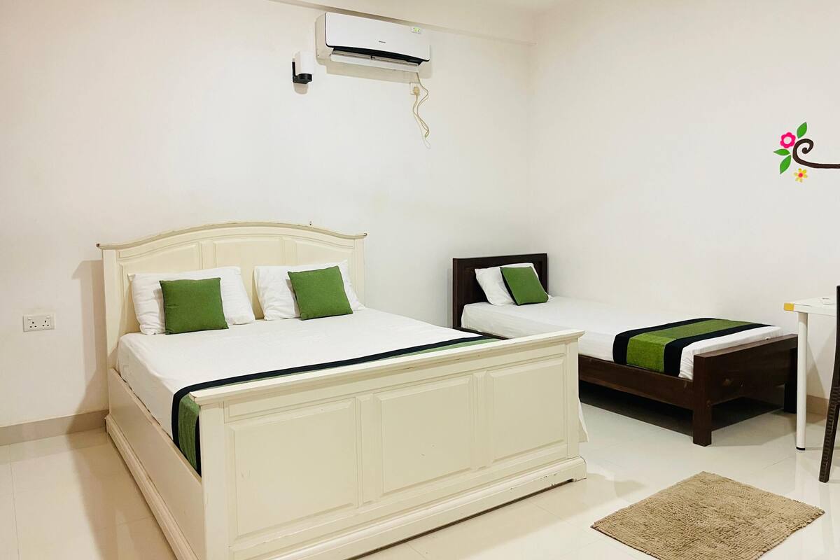 Quarto com duas camas, ar condicionado, escrivaninha e um tapete pequeno.