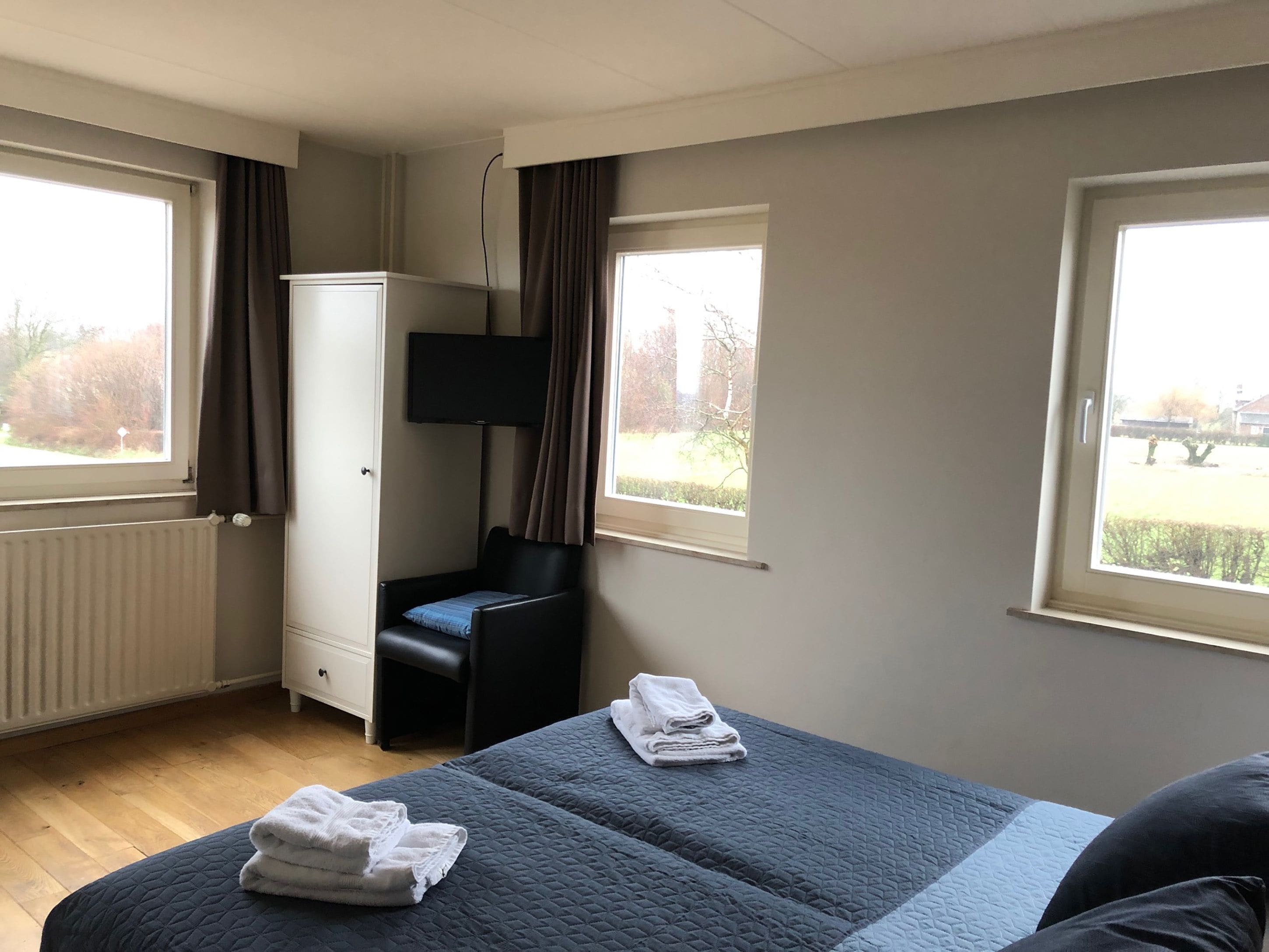 Quarto de hotel com uma cama, uma cadeira, uma televisão e uma janela com cortinas.
