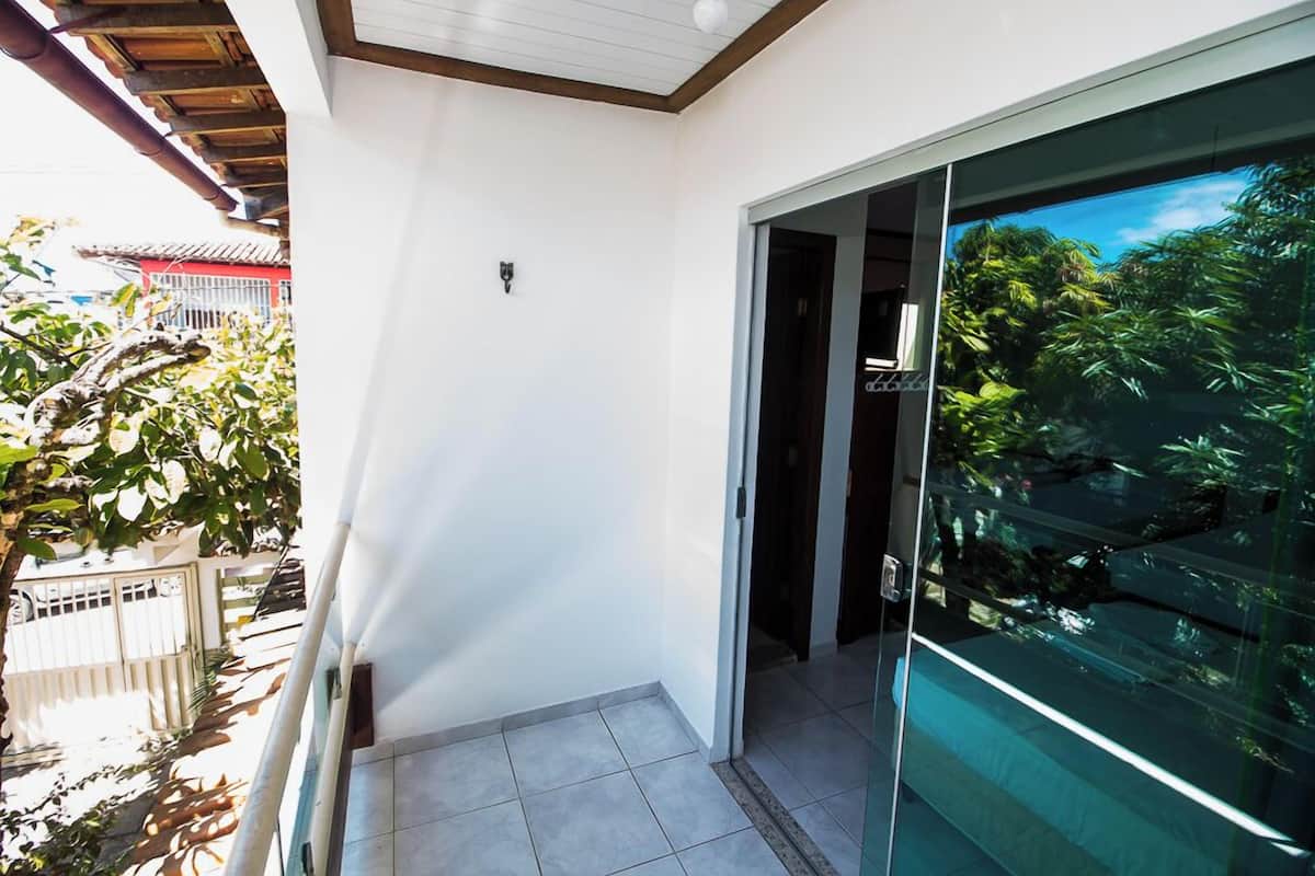 Varanda com porta de vidro que dá para um quarto, chão de azulejos e vista para o verde.