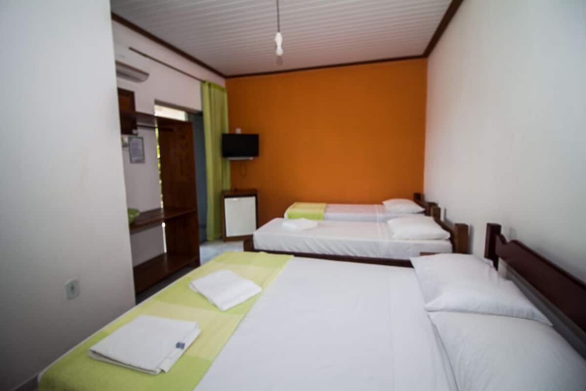 Quarto de hotel com duas camas de solteiro, uma televisão na parede e uma cortina verde.