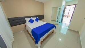 Quarto com cama, cabeceira e banheiro visível através de uma porta de vidro.