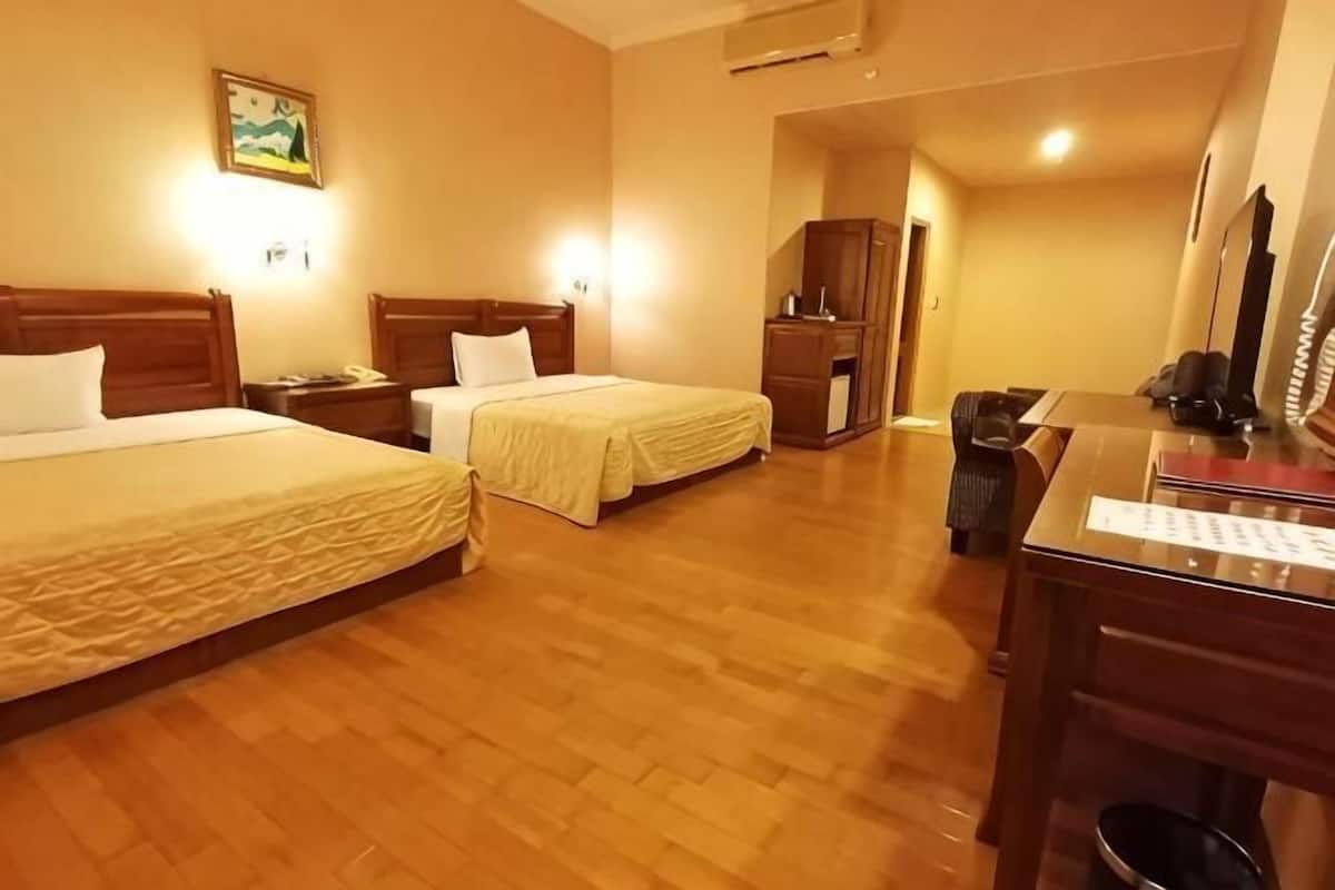 Quarto de hotel com duas camas, uma escrivaninha, uma cadeira, televisão e uma kitchenette pequena.