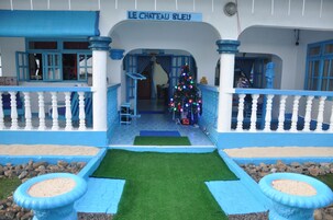 Entrada de um hotel com fachada azul e branca, uma árvore de Natal e uma placa com a inscrição "LE CHATEAU BLEU".